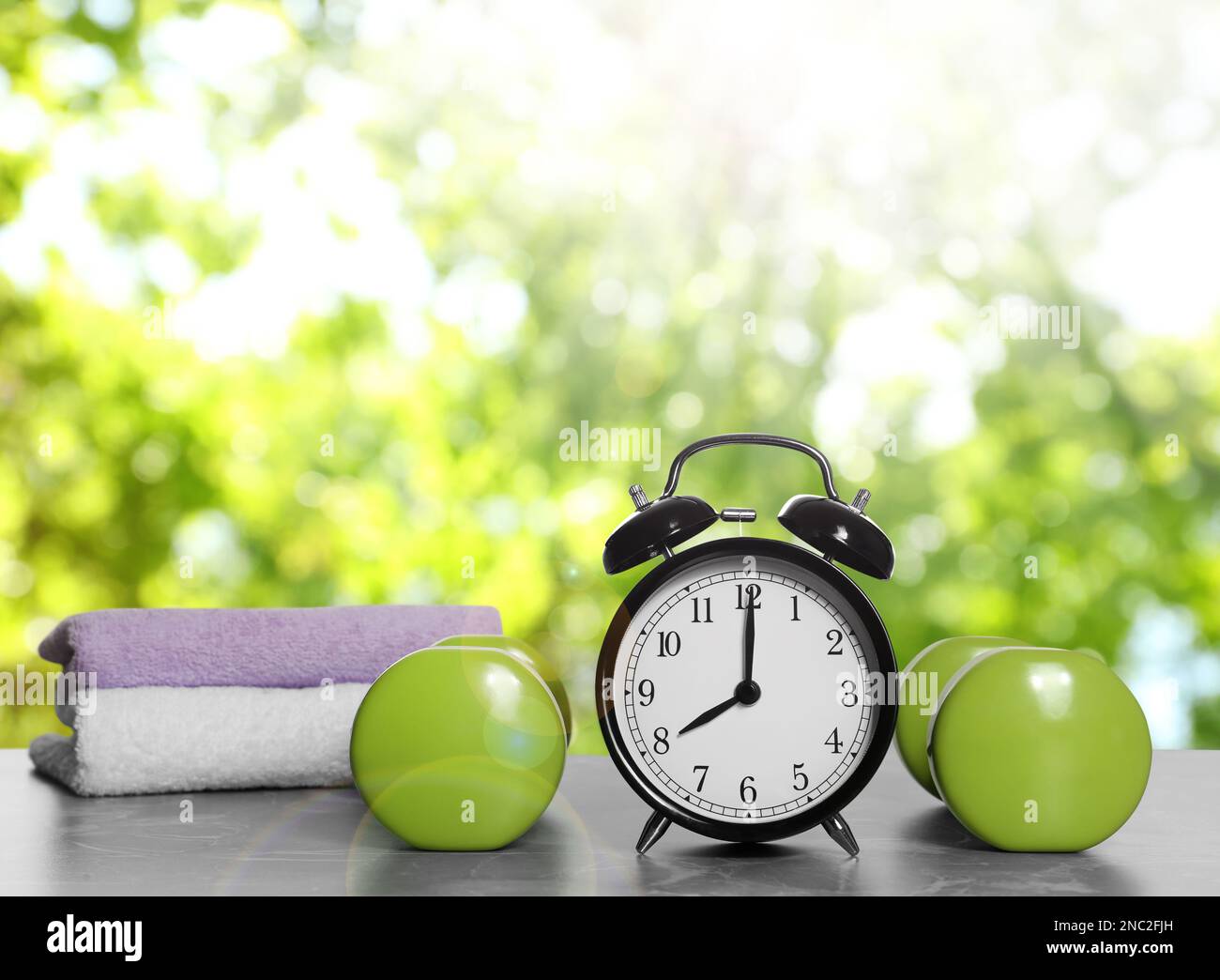 Alarm clock and dumbbells on marble table outdoors. Morning exercise ...
