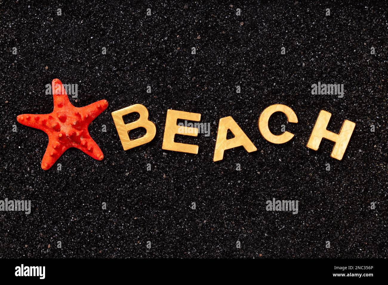 Beach - Golden letters in black sand and red starfish Stock Photo - Alamy