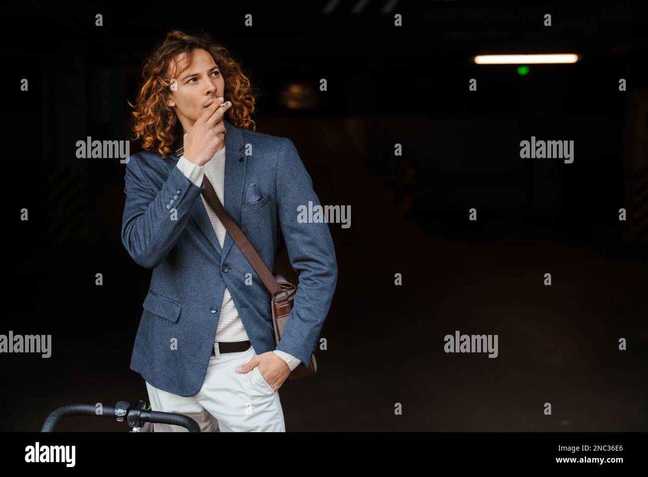 Young ginger long-haired man wearing jacket smoking cigarette outdoors ...