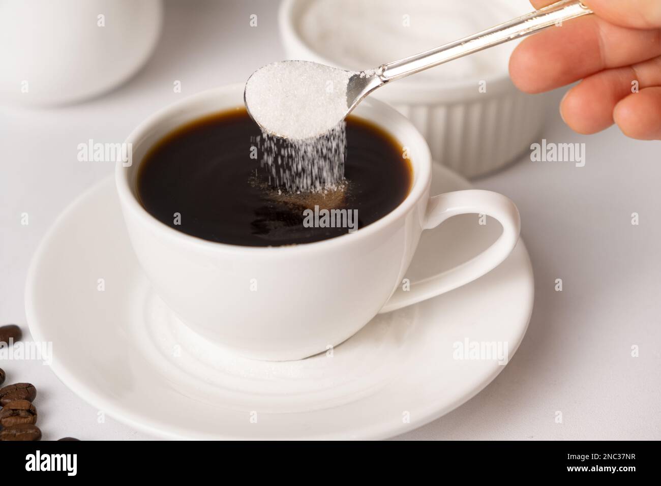 The process of pouring white sugar from a spoon into a white cup of ...