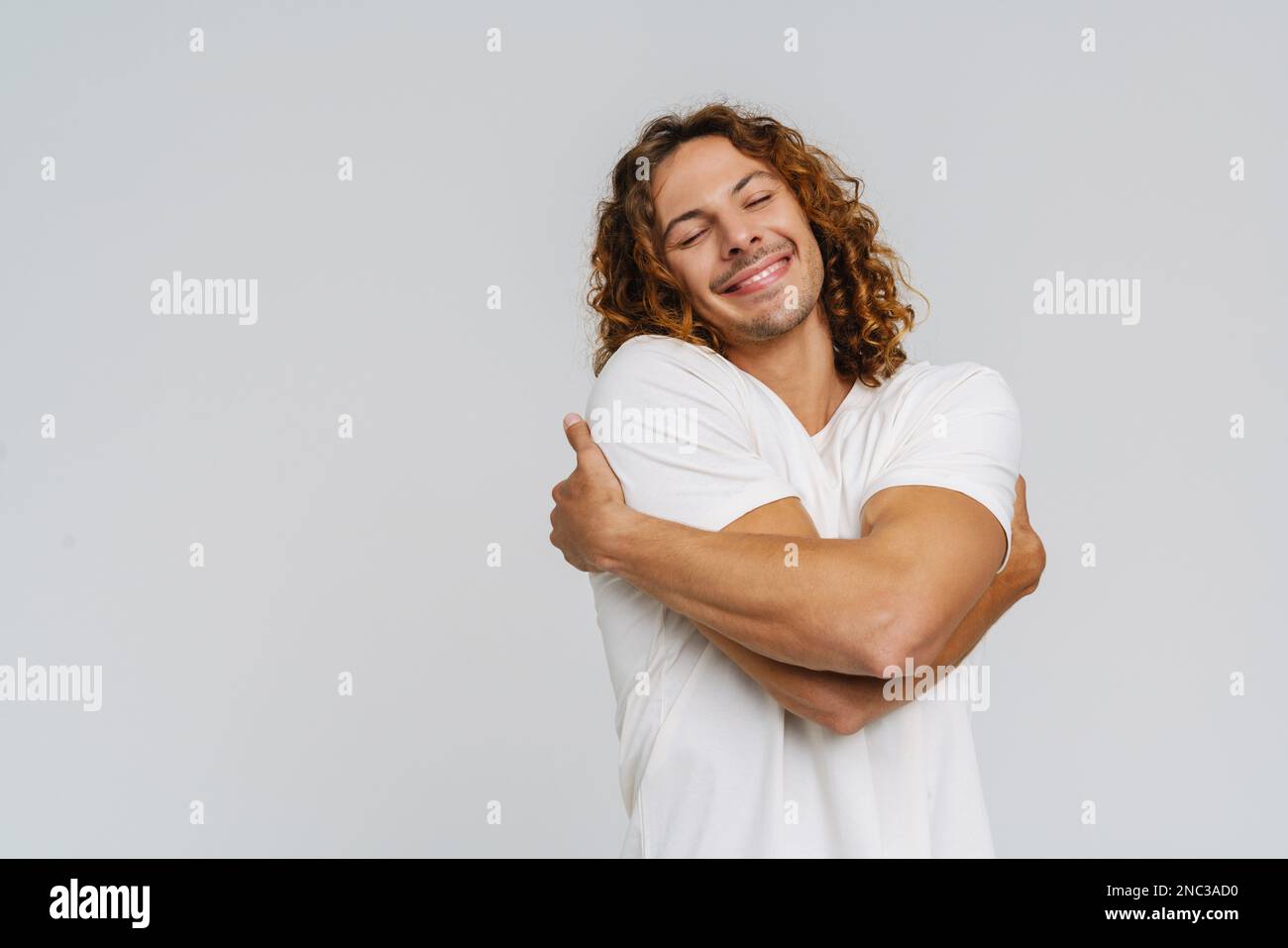 Ginger european man smiling while hugging himself isolated over white ...