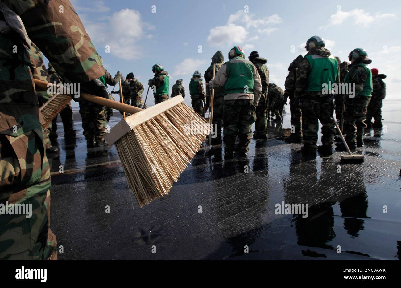 U.S. Navy crew members wait for the order to mop up the flight deck to ...
