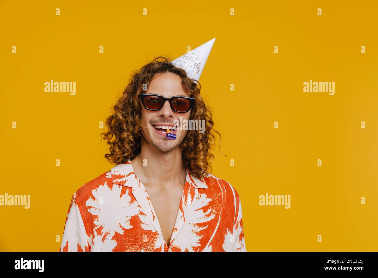 Ginger man in party cone laughing while posing with birthday whistle ...