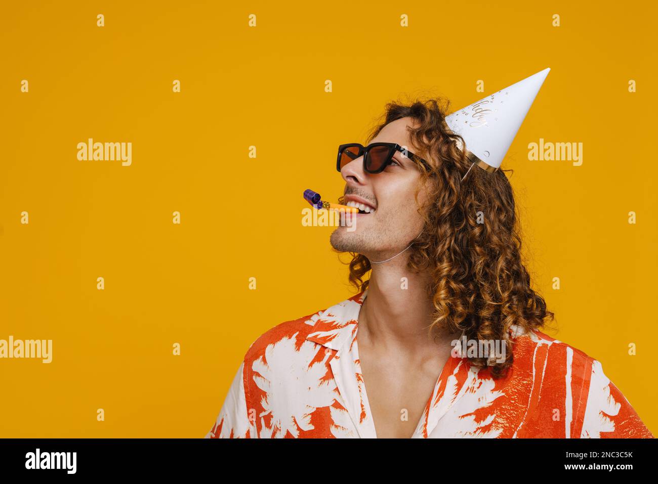 Ginger man in party cone laughing while posing with birthday whistle ...