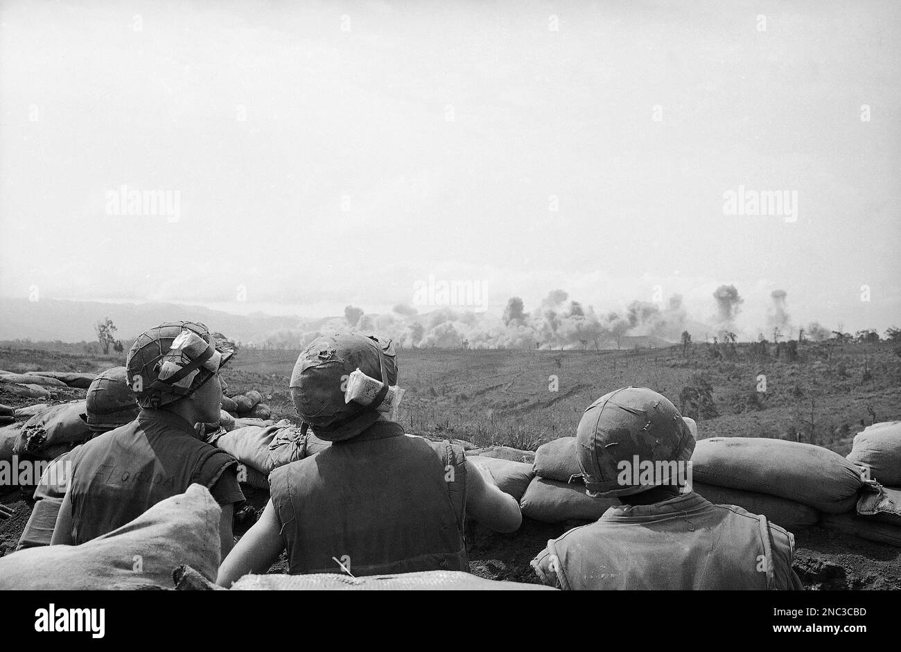 U.S. Marines in sandbagged trenches watch smoke rise from a B52 strike ...