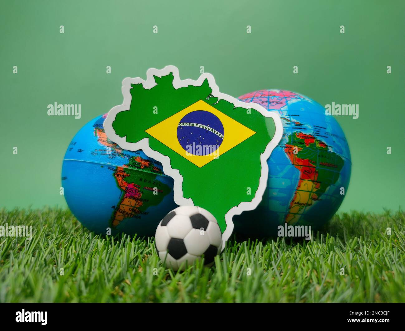 A ball and brazil flag sticker on a green field with a blurred globe ...
