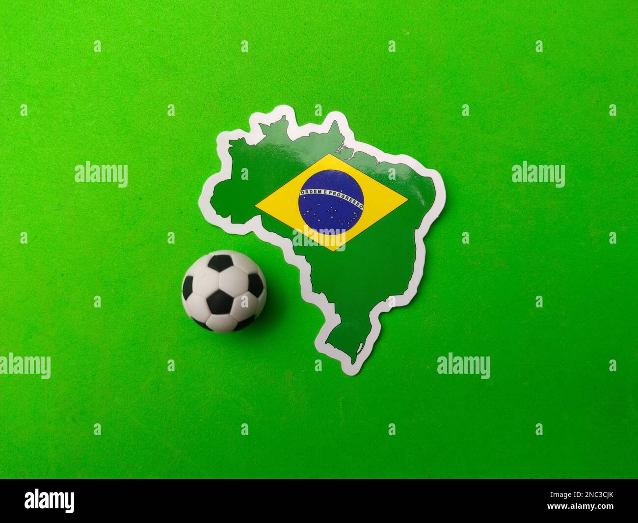 A ball and brazil flag sticker on a green background with copy space ...