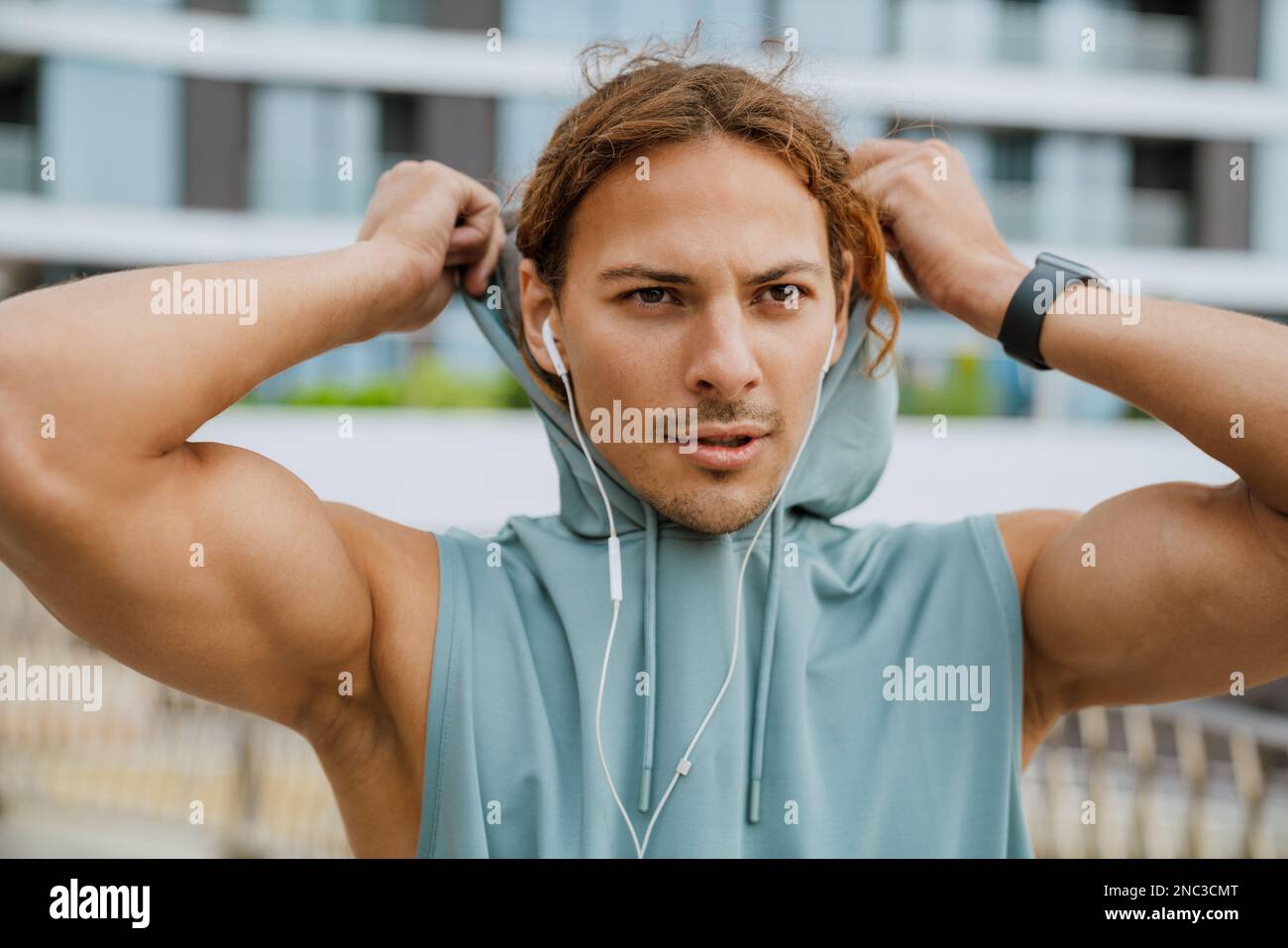 Young athletic long-haired serious handsome man putting on the hood and ...