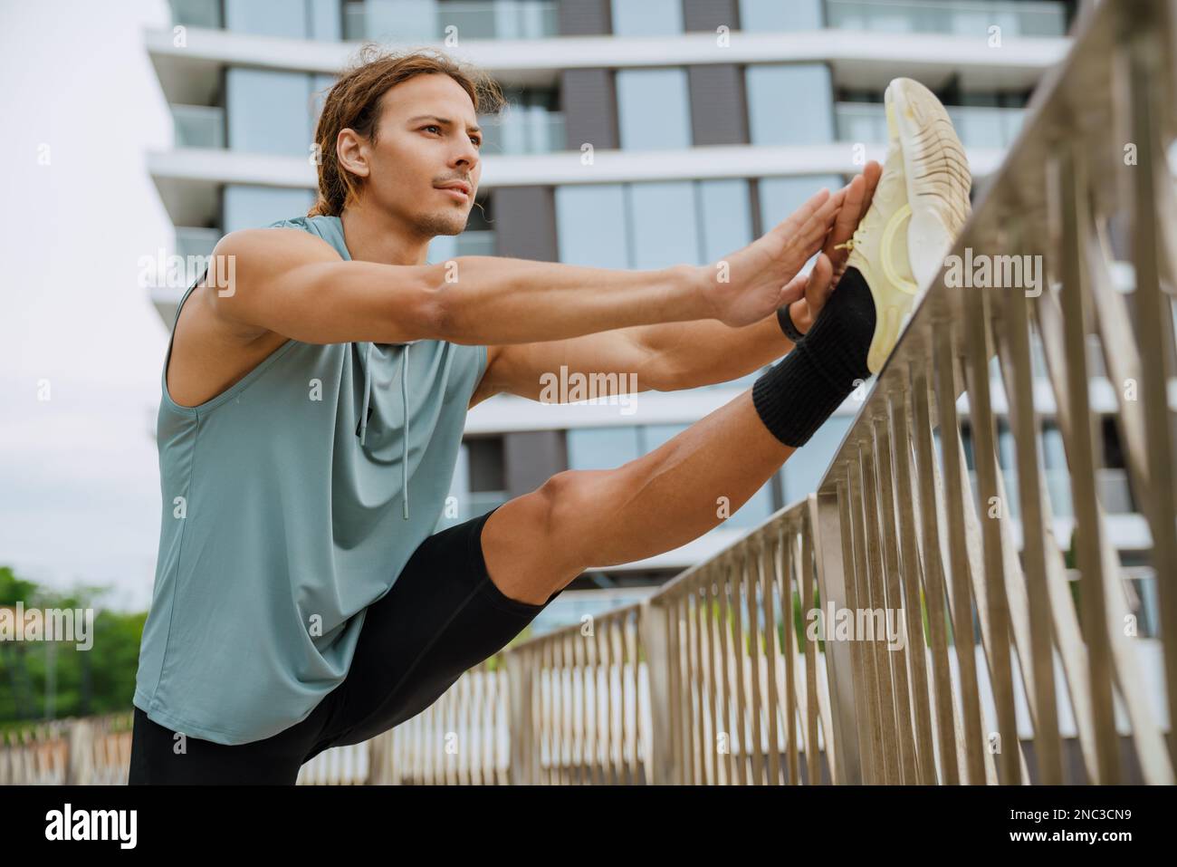 Young athletic long-haired serious handsome man stretching his leg on ...