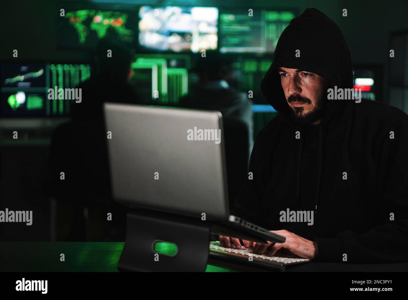 Hooded male criminal hacker using a laptop to breack the security of ...