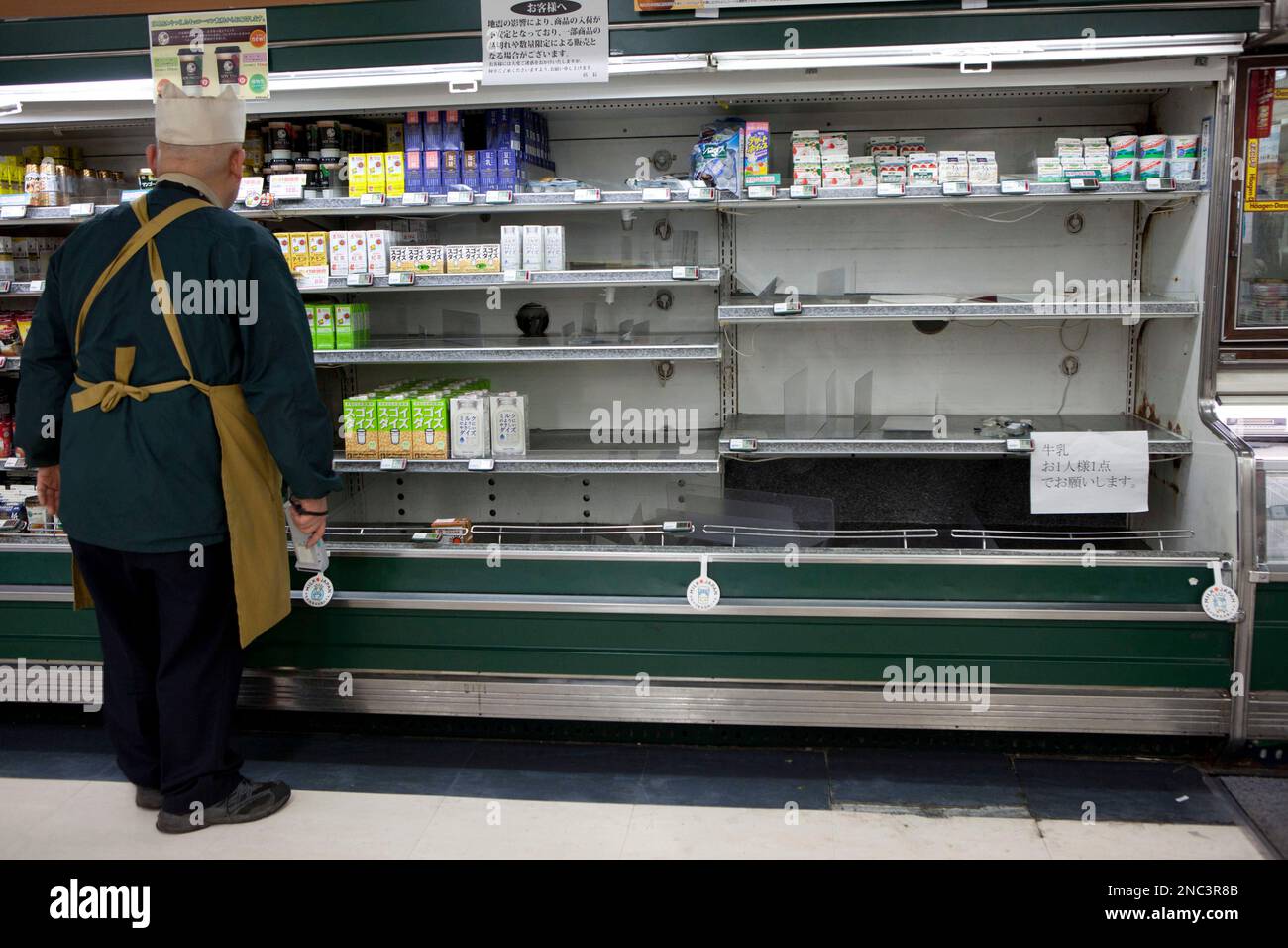 A Japanese grocer stands near the empty milk section of a supermarket ...
