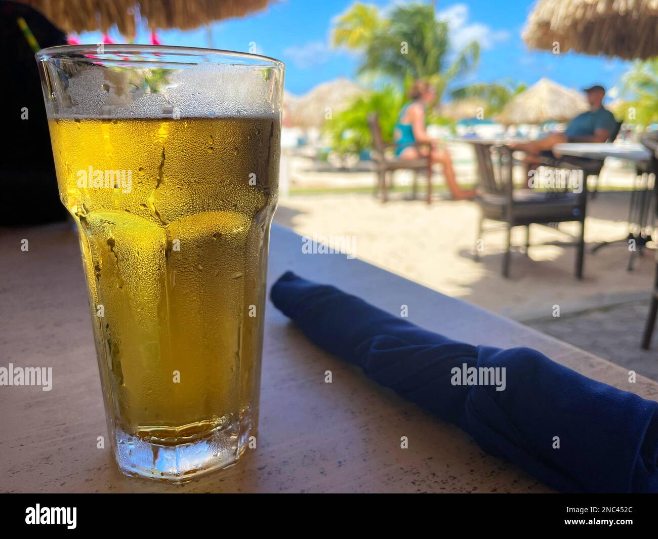A glass of cold beer, condensation running down the sides, on a table ...