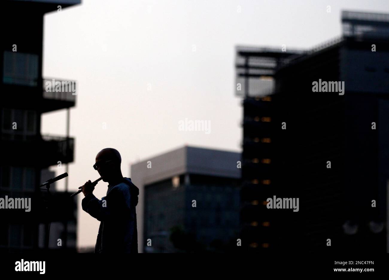 George Abe is silhouetted as he plays yokobue, a Japanese flute, during ...