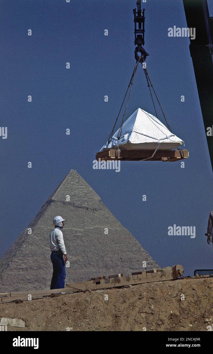 A construction worker supervises a crane as it hoists the capstone of a ...