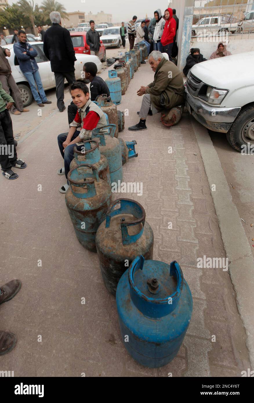 Libyans wait by empty cooking gas cylinders as they queue in front of a ...