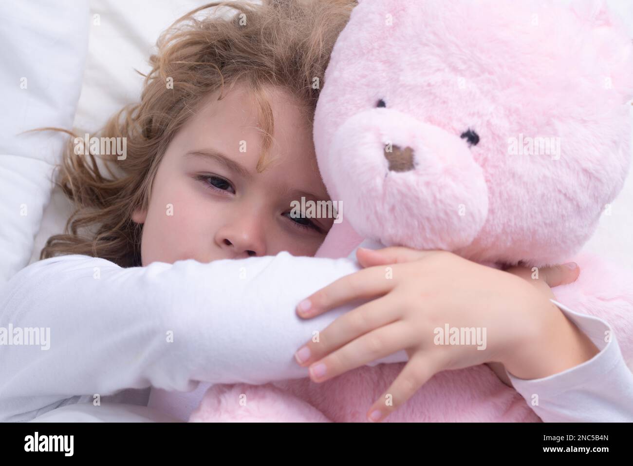 Child wakes up with toy teddy bear from sleep in bed. Kid wakes up in ...