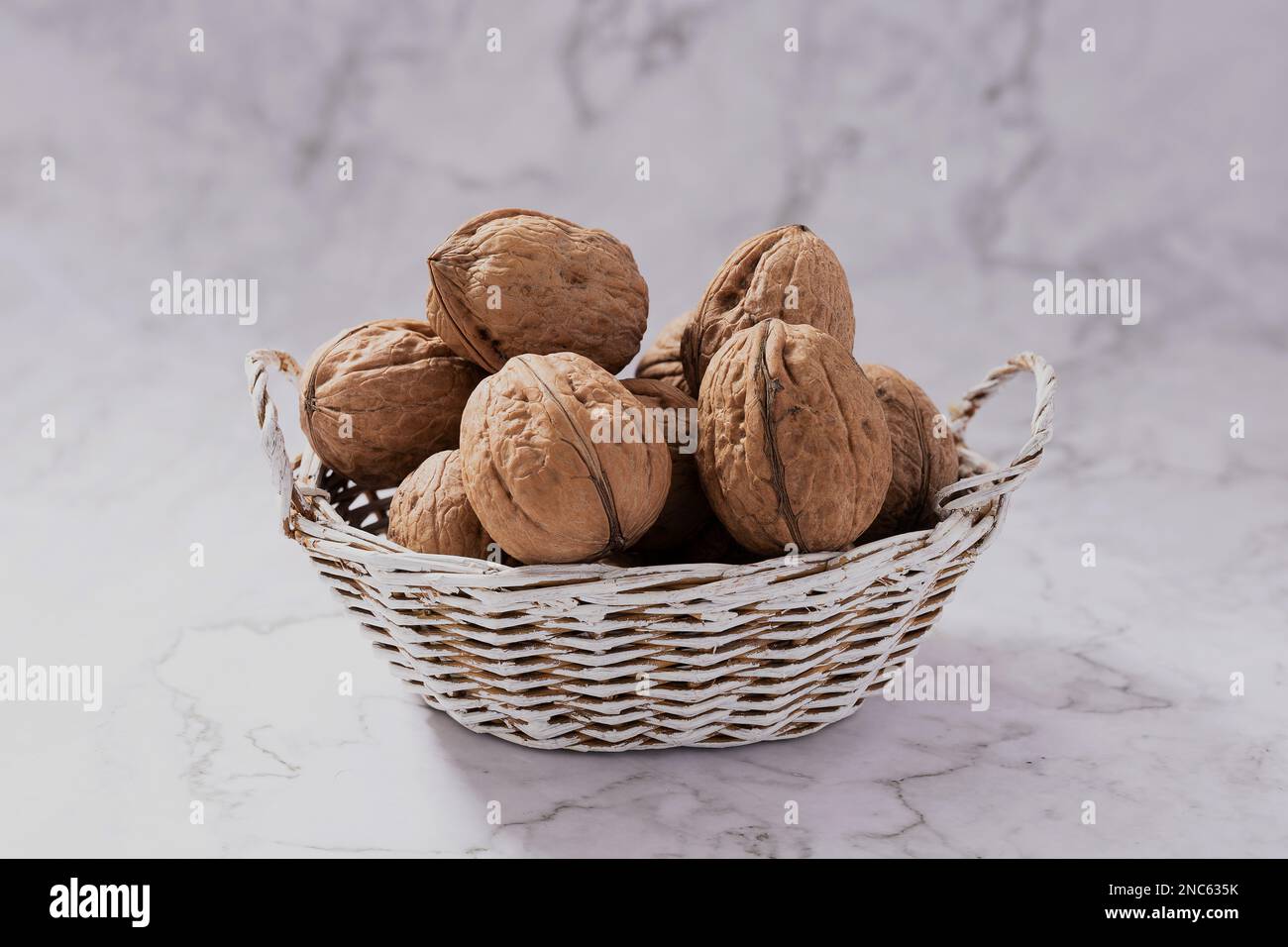 Raw walnut in shell inside a wicker basket on white background, closeup ...