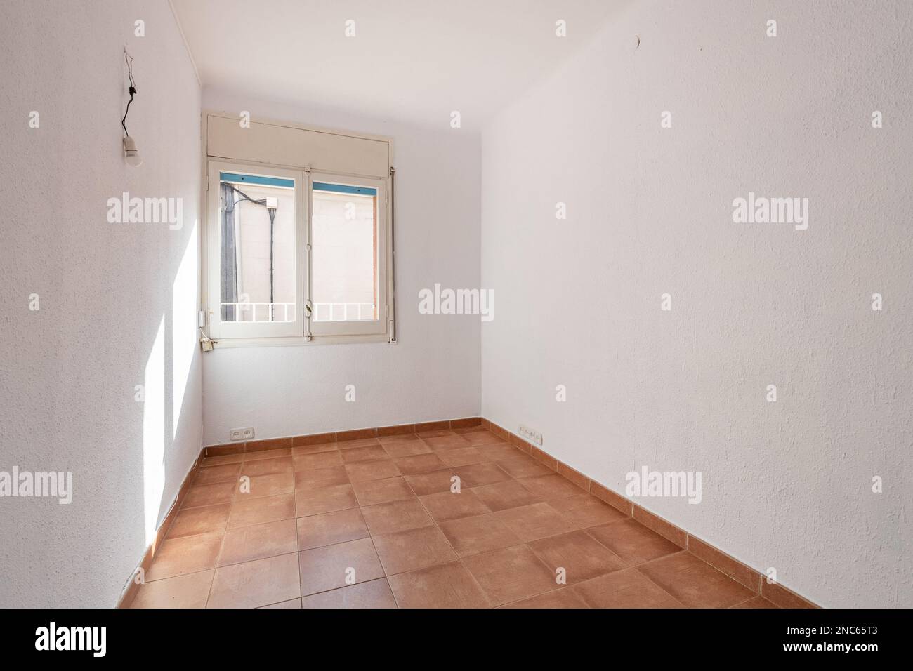 An empty spacious room with old square worn caramel colored floor tiles ...