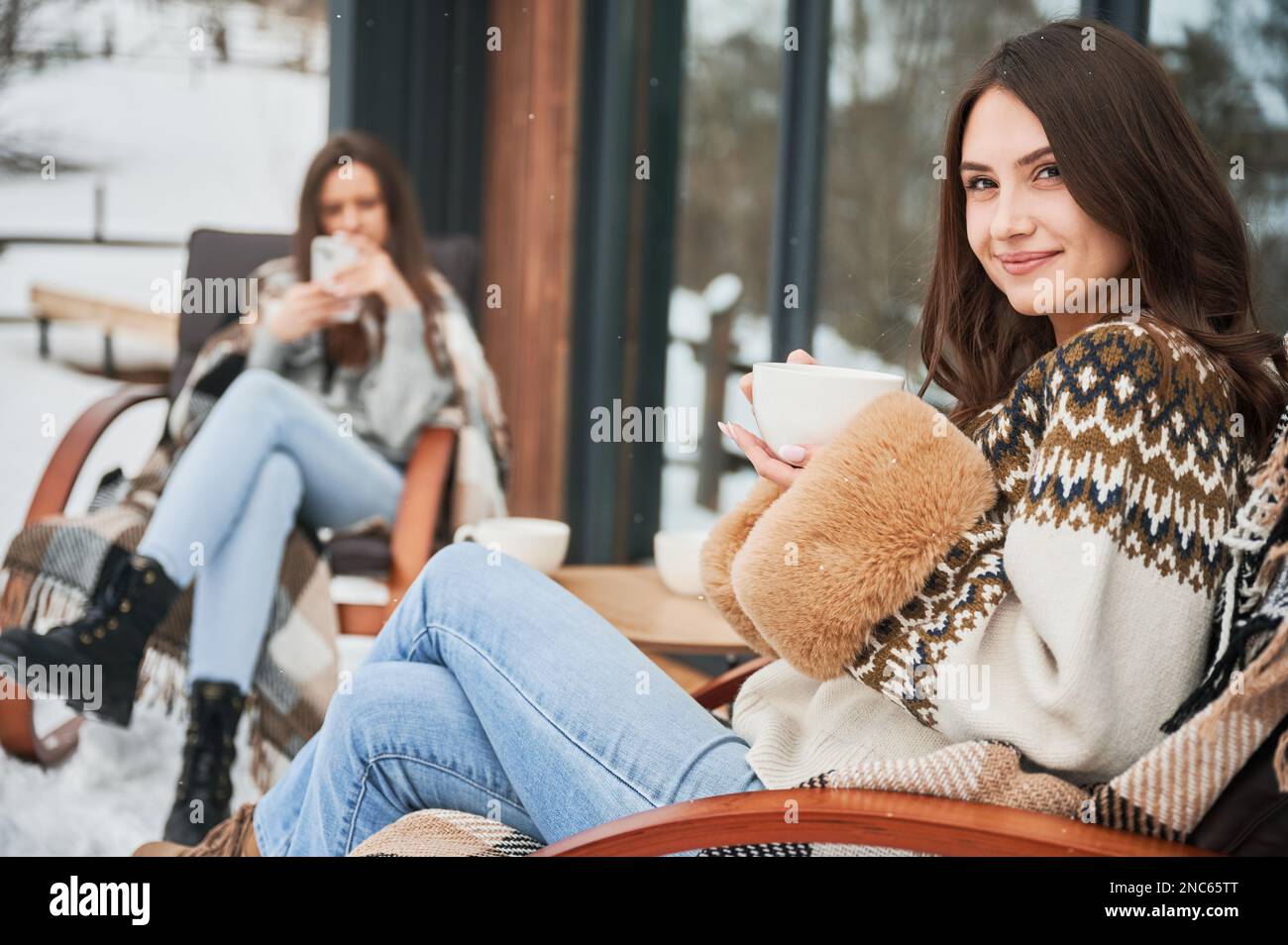 Young women enjoying winter weekends on terrace of contemporary barn house in the mountains. Two ...