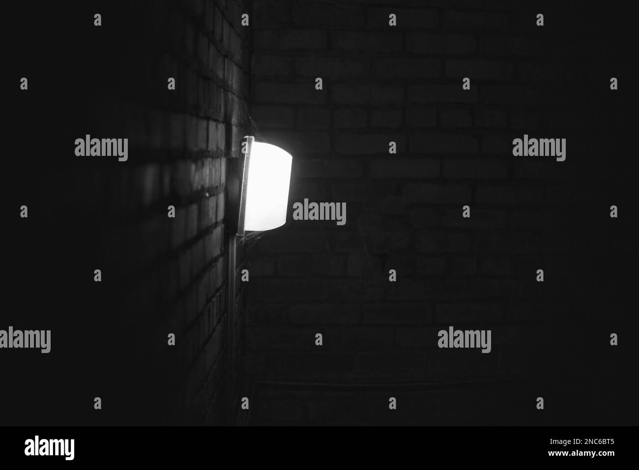 Single hallway wall sconce lamp shining in the darkness in a black and ...