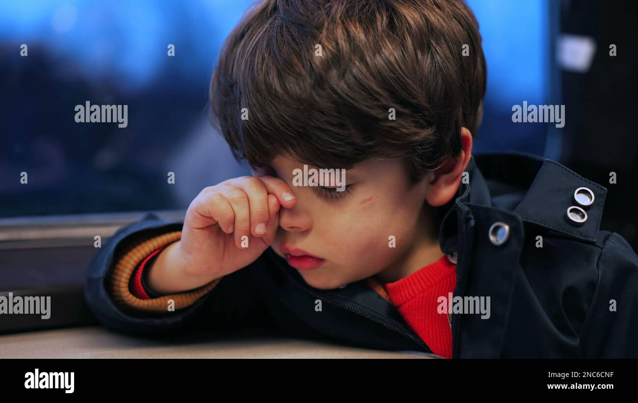 Tired small boy rubbing eye with hand feeling exhausted while traveling ...