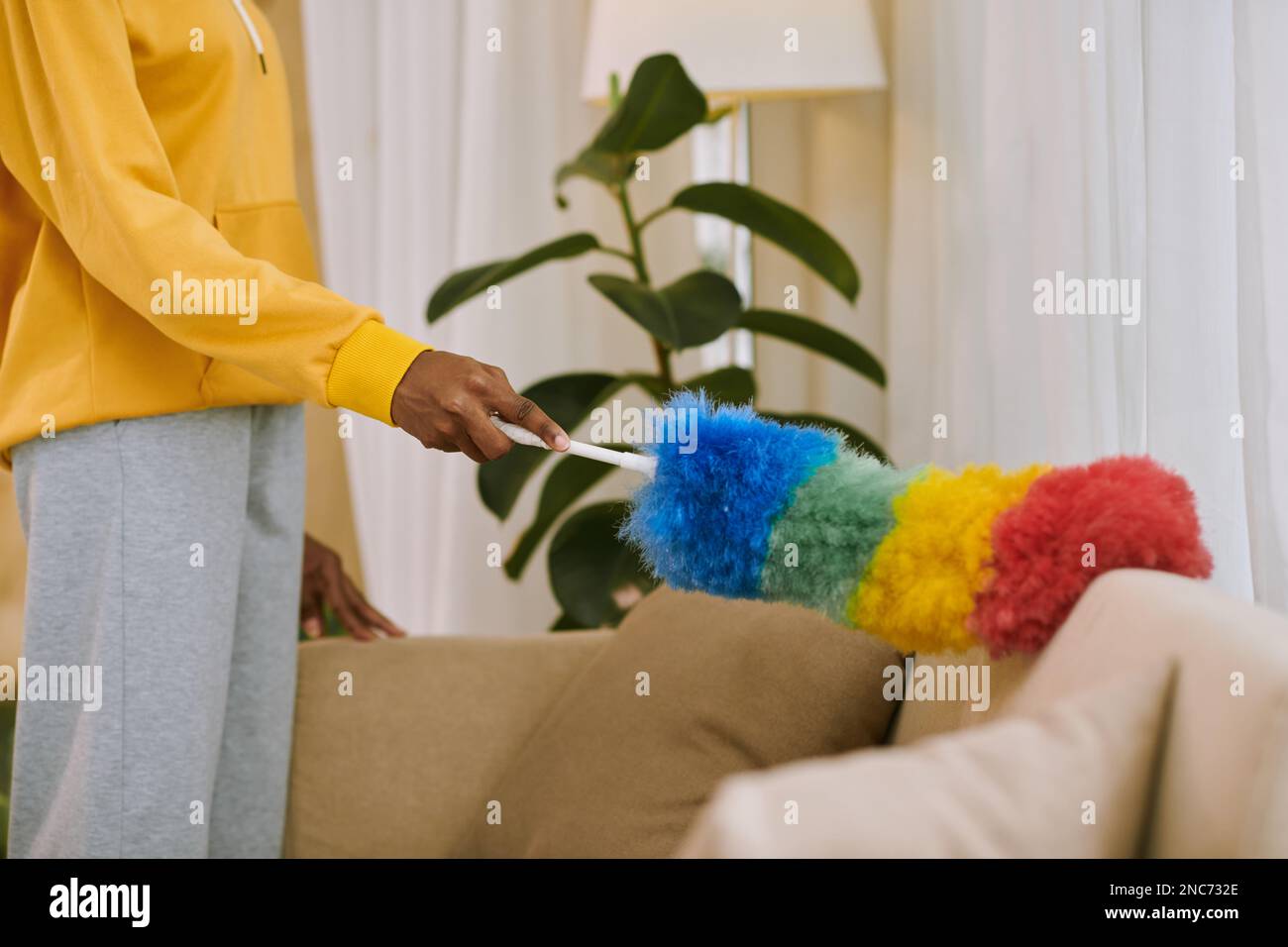 Young woman using static duster when brushing dust off couch Stock ...
