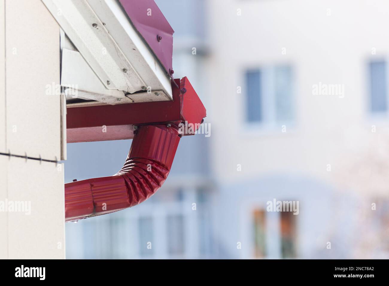 A drop of melting snow on the red roof gutter of a building against the ...