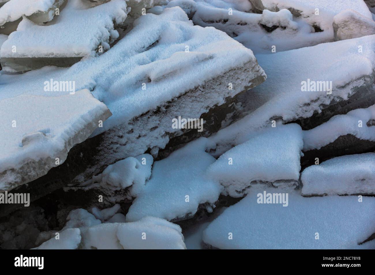 Huge broken ice blocks lie on the river bank under the snow. Spring ...