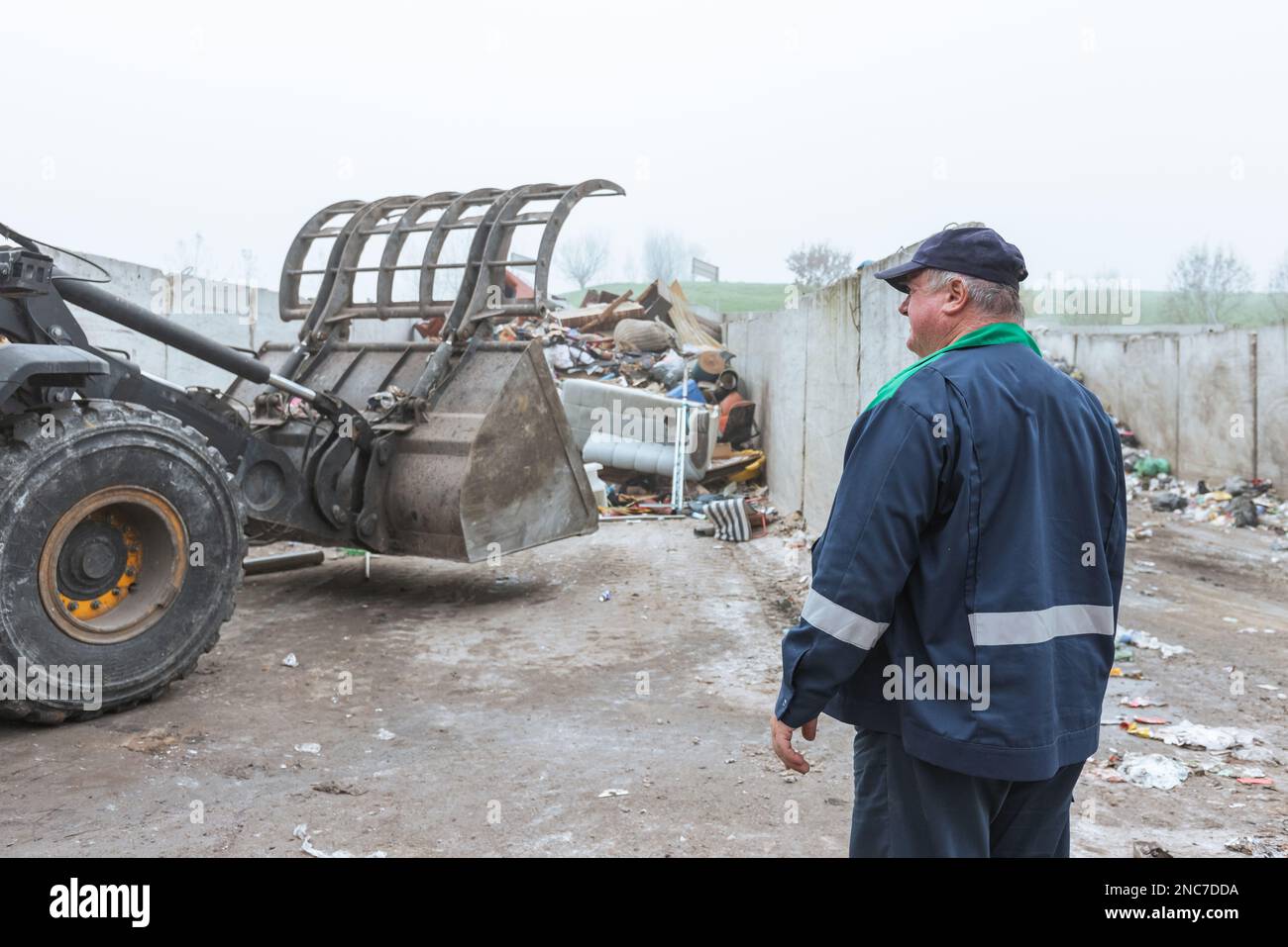 Recycling center worker, in dark blue work clothes, looking at an ...