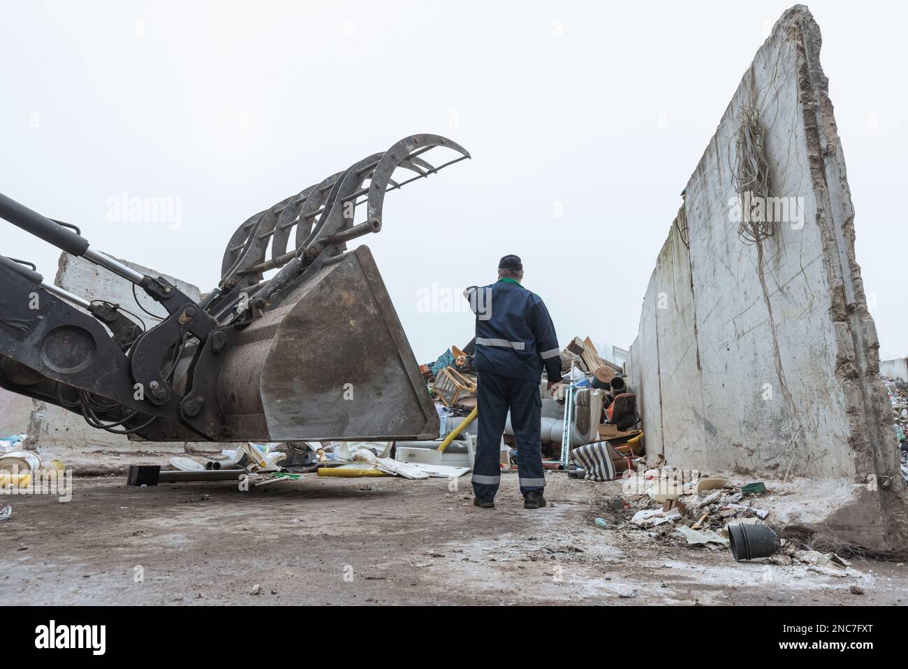 Male worker pointing on wheel loader and the garbage heap at a landfill ...