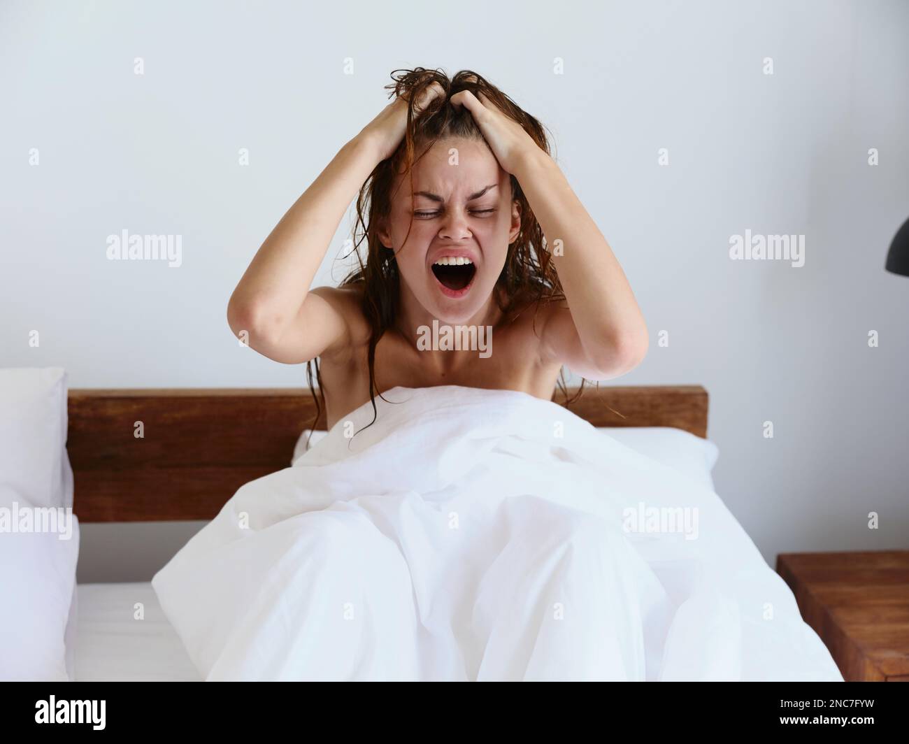 An angry woman sits on a bed in the bedroom and covers her body with a blanket, early awakening ...