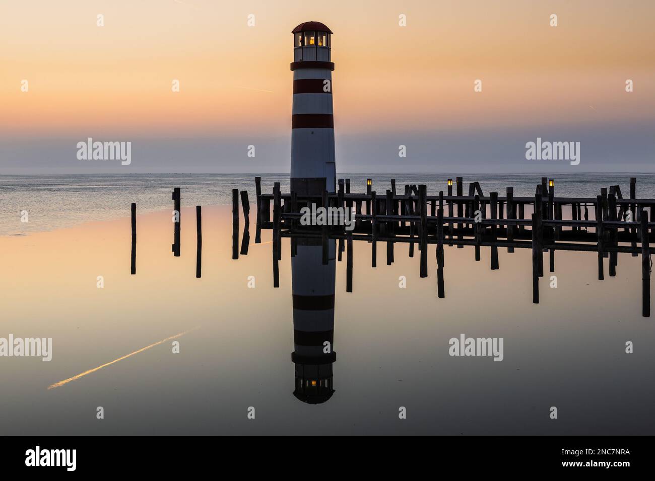A lighthouse on pier reflecting in the water at sunset Stock Photo - Alamy
