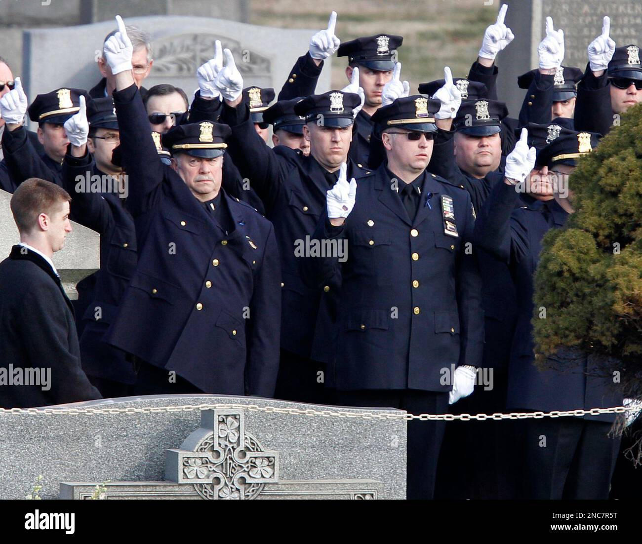 Police officers hold their gloved fingers in the air at the burial of ...