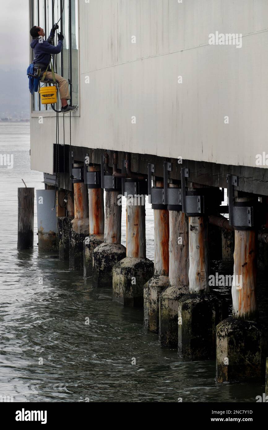 Wooden pilings support waterfront buildings as a window washer hangs ...