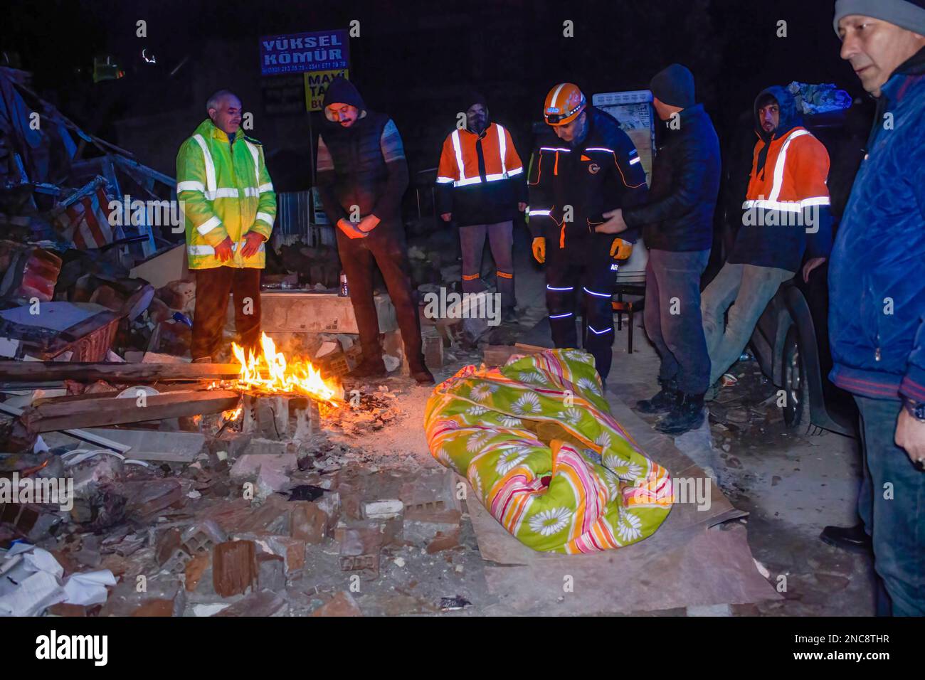 Earthquake survivors and Rescue team members warm up by a fire. Turkey ...