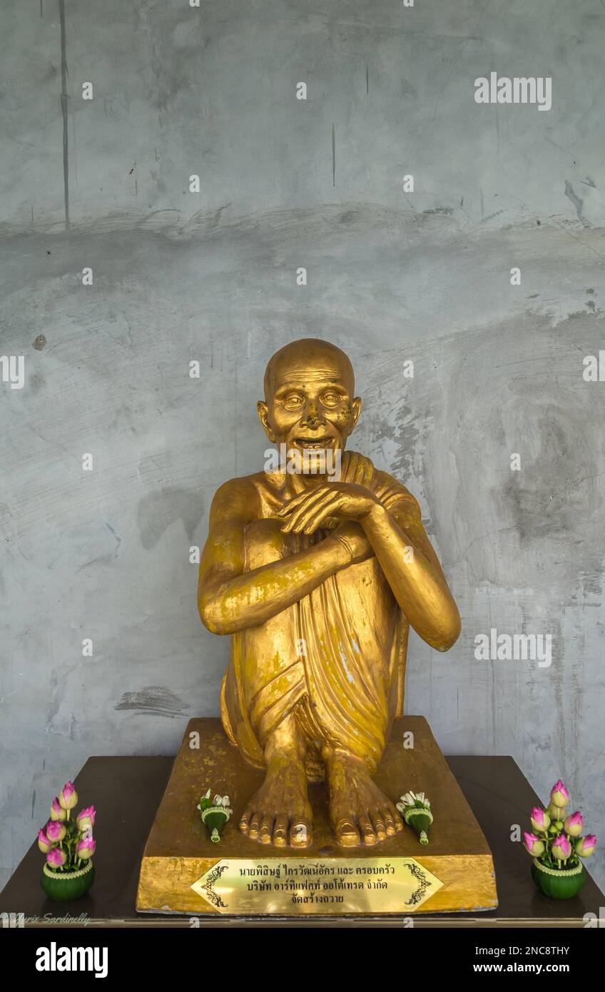 A vertical closeup of a golden sitting monk statue in a thai temple ...
