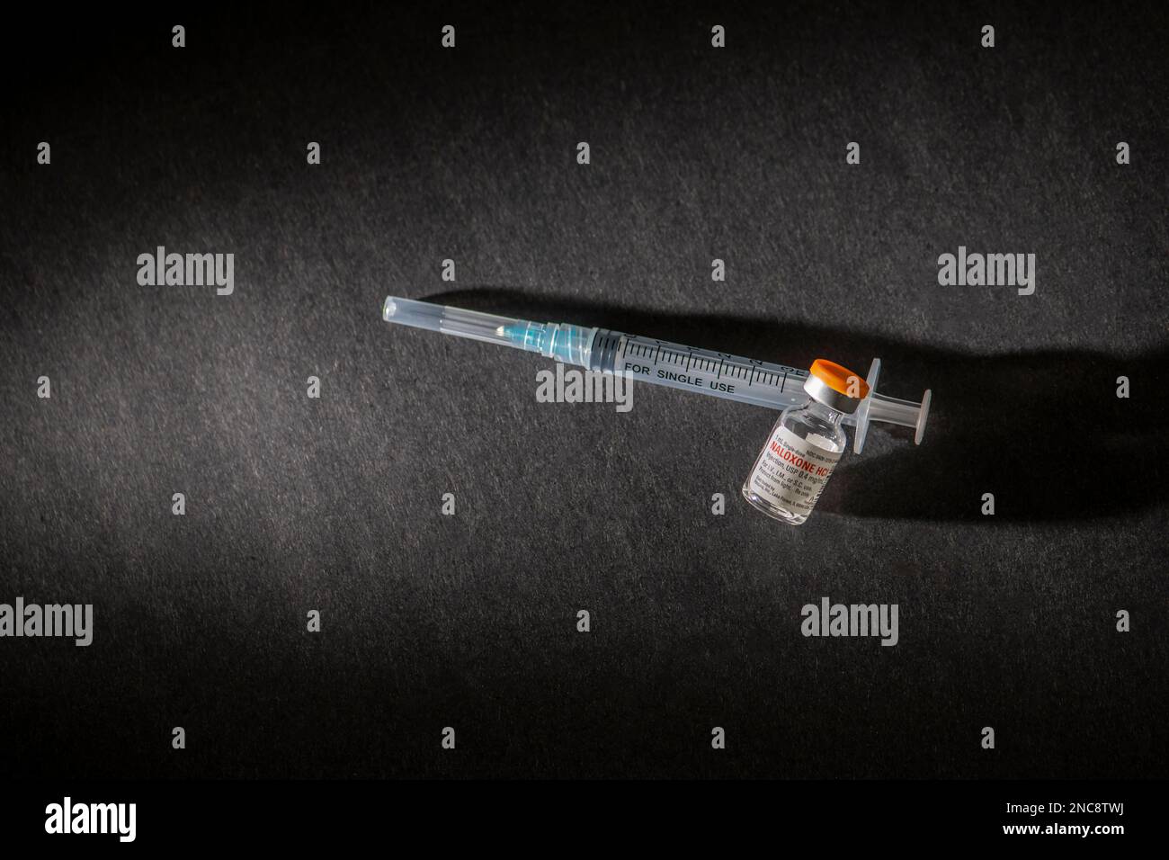 A dramatic view of a bottle of Naloxone with needle on a black ...