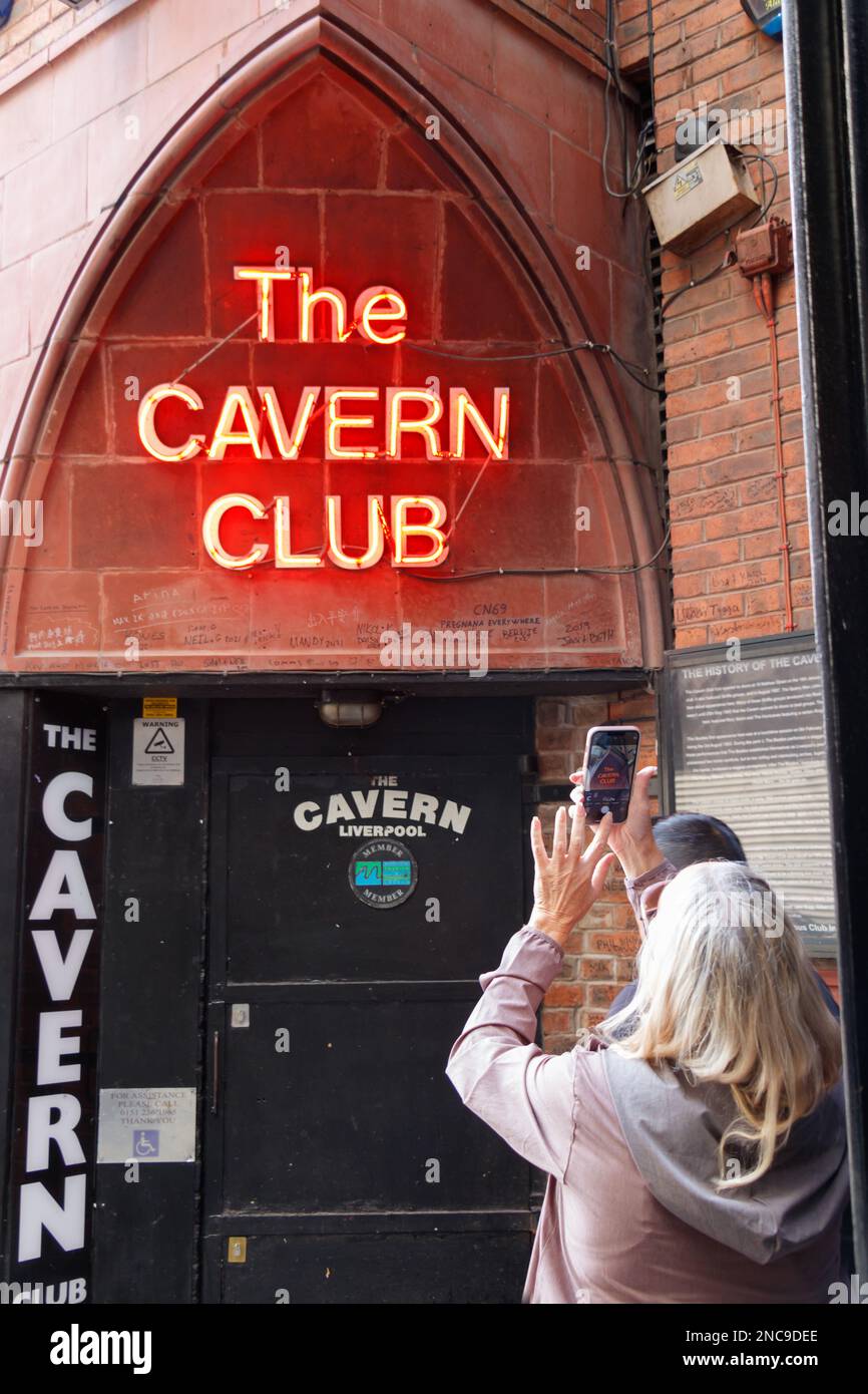 female tourist photographing neon sign and doors to the Cavern Club ...