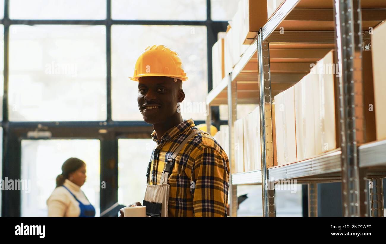Male storage room employee standing near racks filled with goods in ...