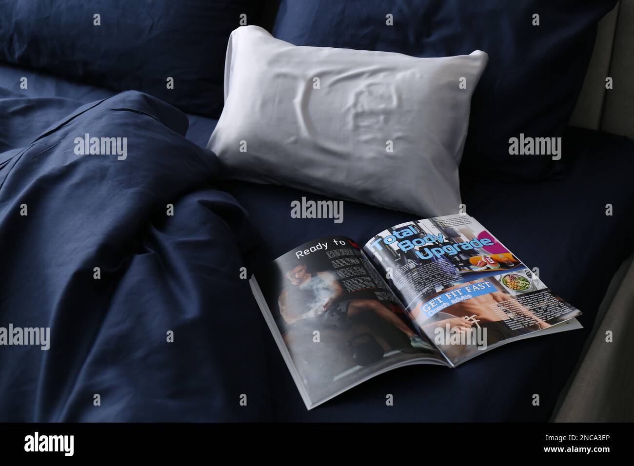 Open magazine on bed with stylish silky linens Stock Photo - Alamy