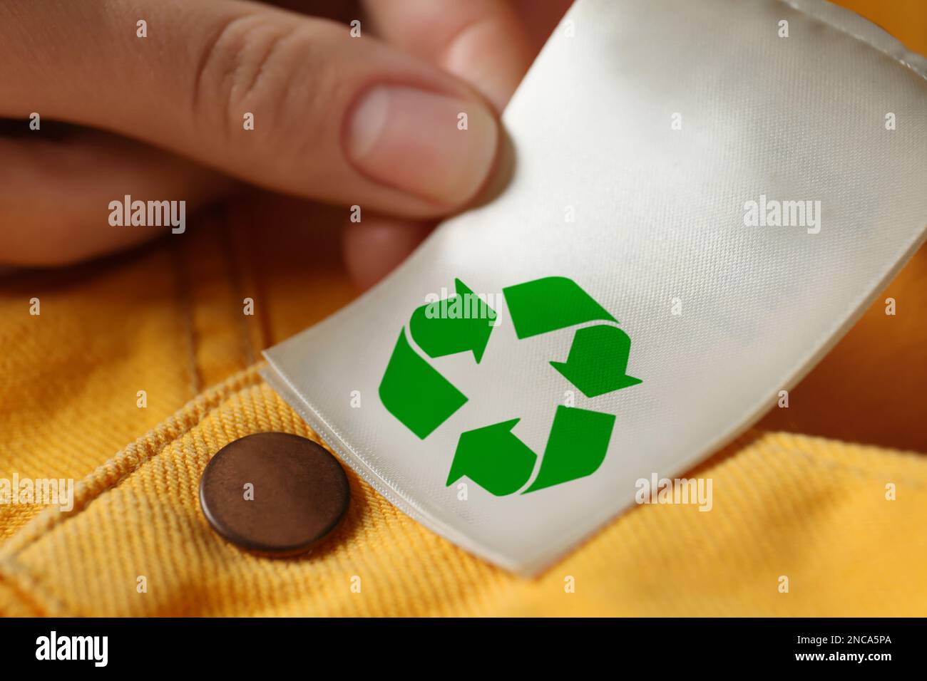 Woman showing clothing label with recycling symbol on yellow jeans ...