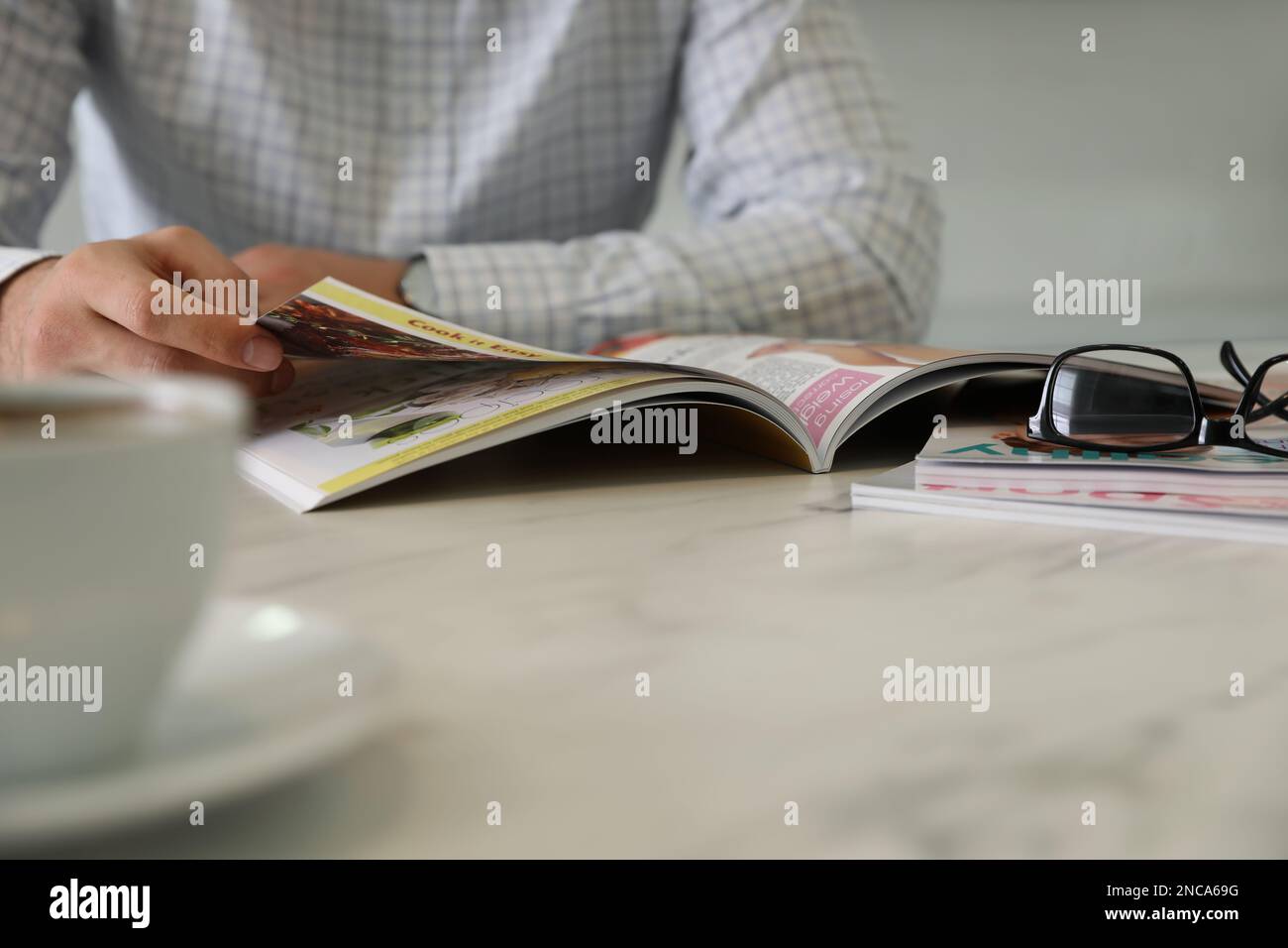 Man reading magazine at white table, closeup Stock Photo - Alamy