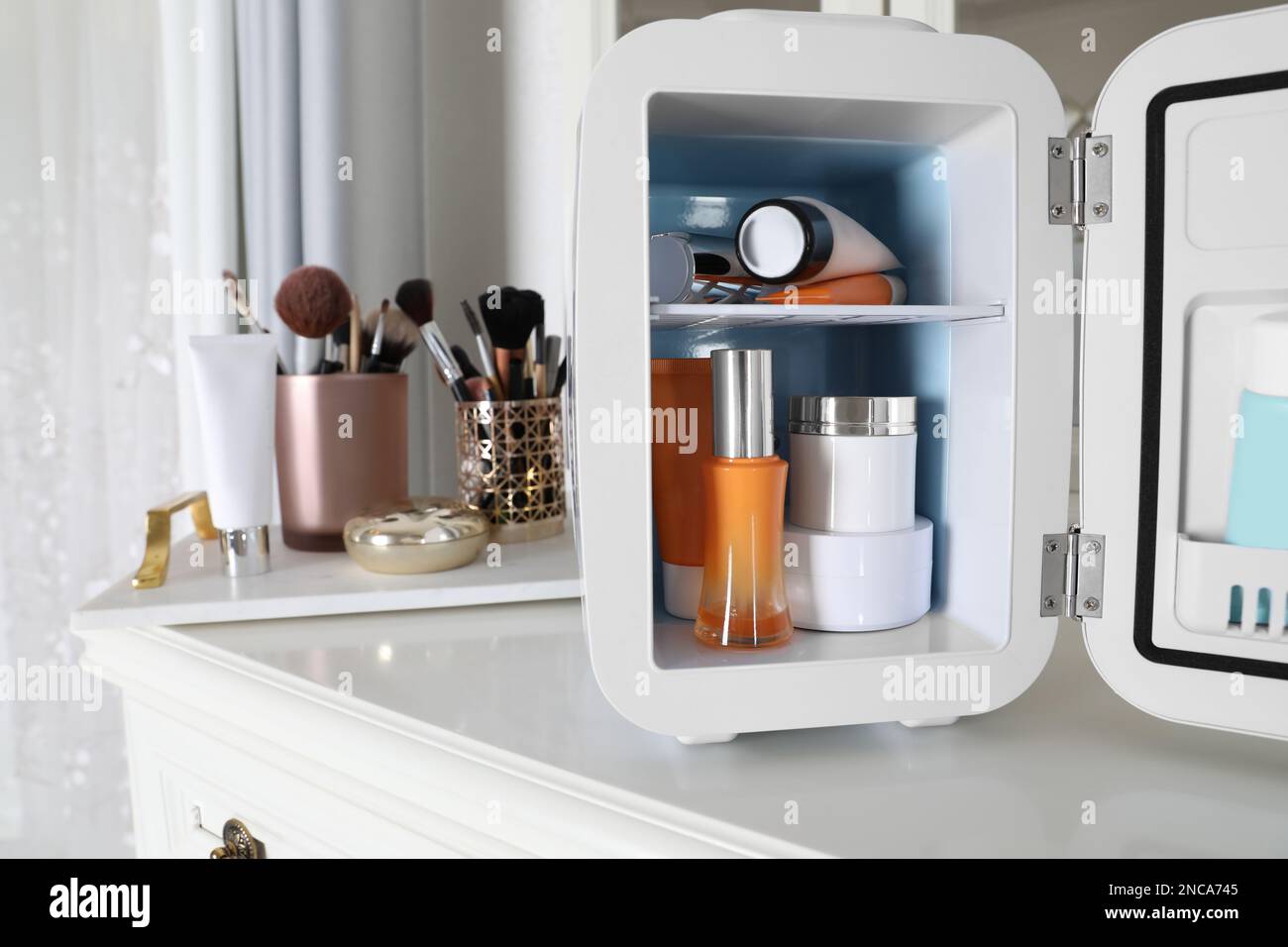 Mini fridge with cosmetic products on white vanity table Stock Photo ...