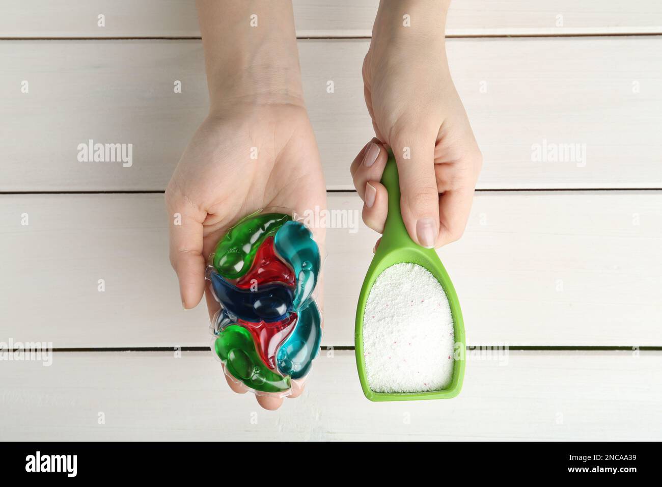 Woman holding laundry capsules and detergent powder above white wooden ...