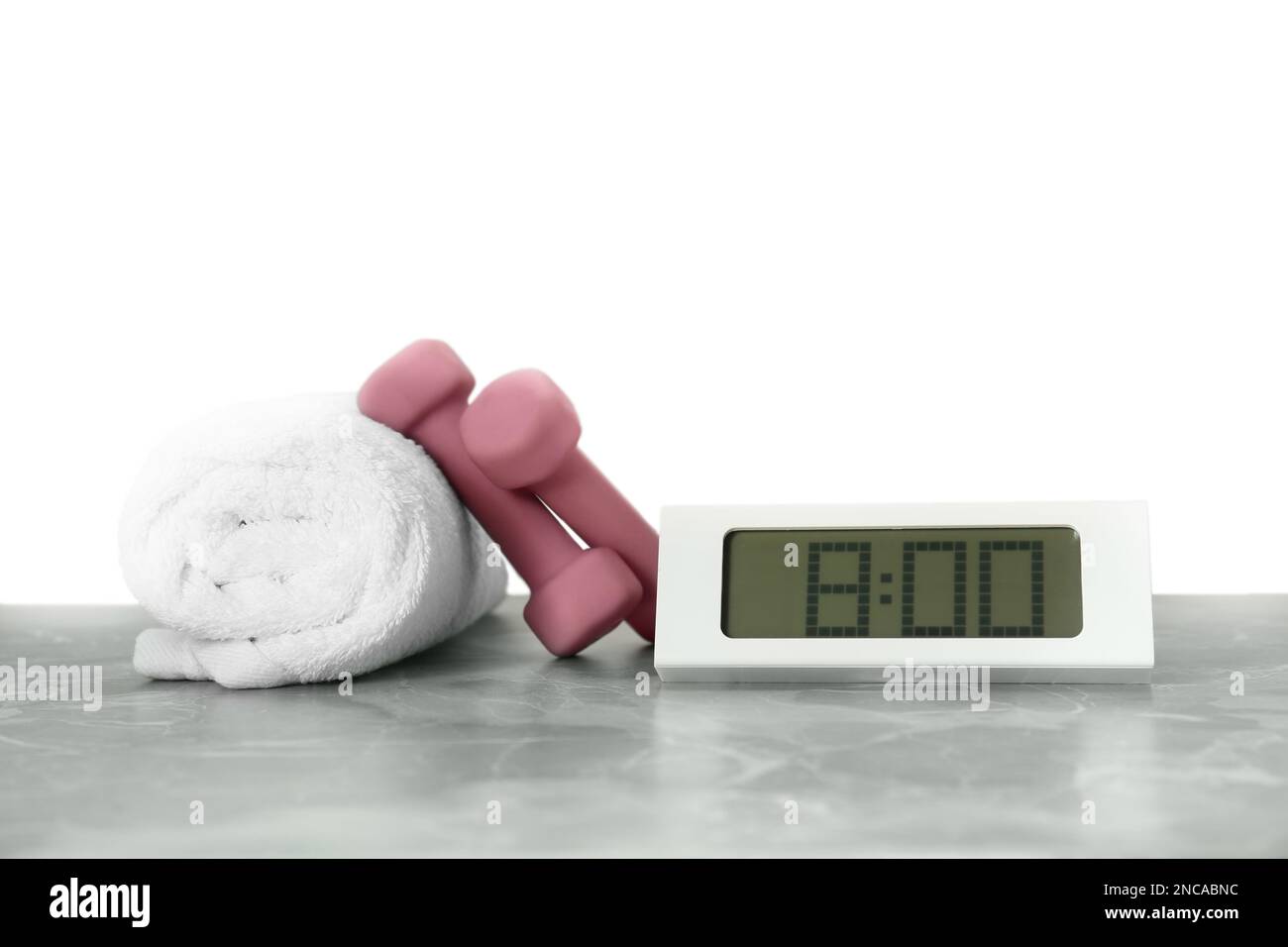 Digital clock, towel and dumbbells on marble table against grey ...