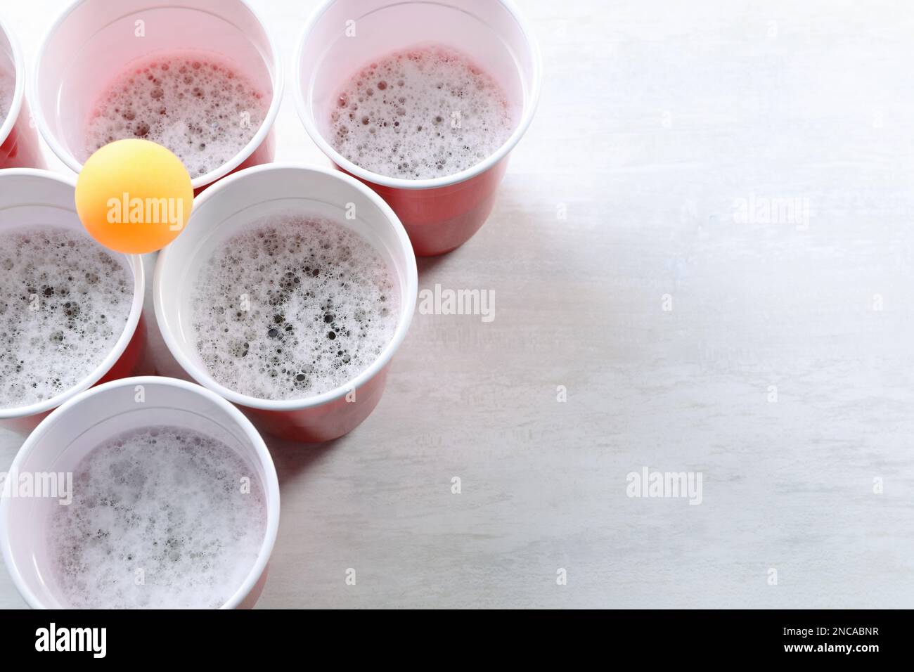 Plastic cups and ball on white table, above view with space for text ...