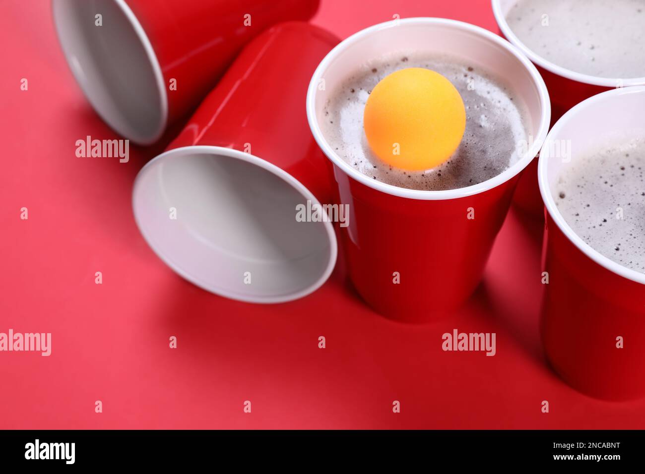 Plastic cups and ball for beer pong on red background Stock Photo - Alamy