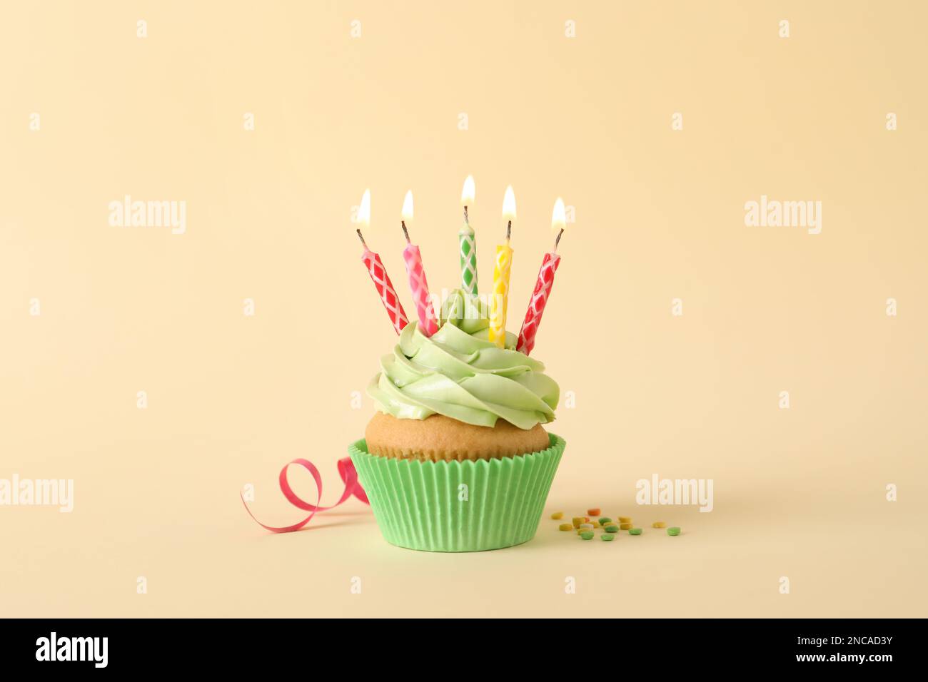 Birthday cupcake with burning candles, streamer and sprinkles on beige ...