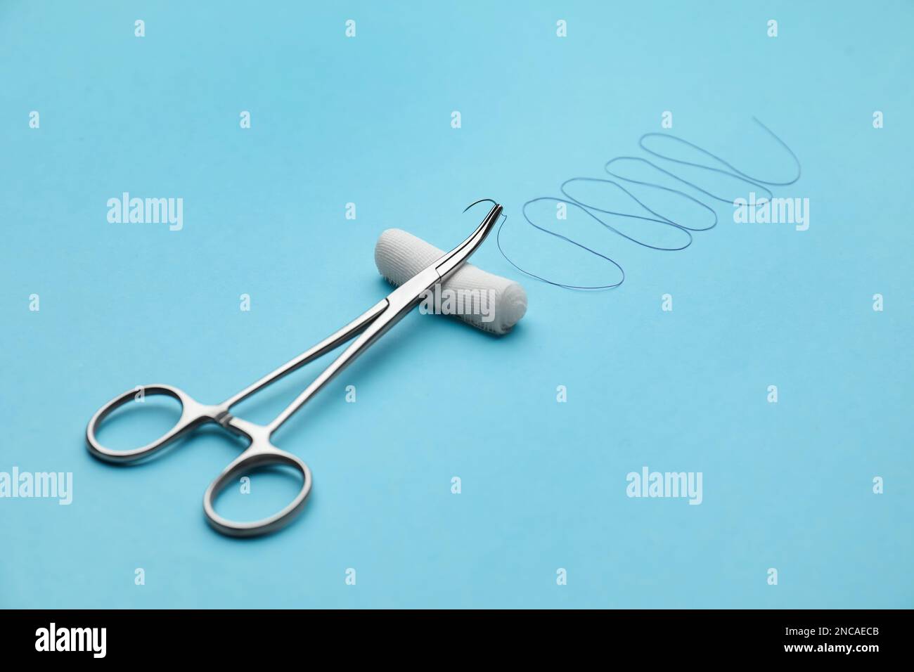 Forceps with suture thread and bandage roll on light blue background ...