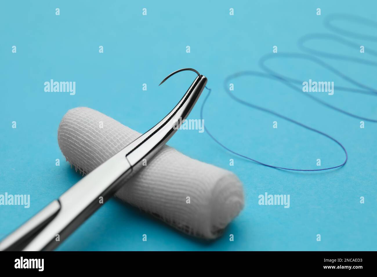 Forceps with suture thread and bandage roll on light blue background ...